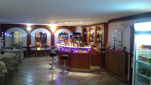 Uma área de bar com balcão, banquetas e uma geladeira repleta de bebidas.