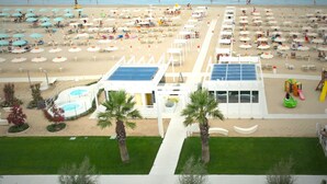 Resort à beira-mar com várias espreguiçadeiras, guarda-sóis, piscina e área de recreação infantil.