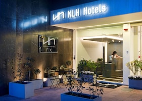 Entrada de hotel com fachada moderna, balcão de recepção e plantas em vasos.