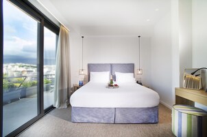 Quarto de hotel moderno com uma cama grande, vista para a cidade e uma varanda.