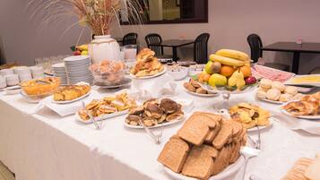 Uma mesa de buffet com diversos alimentos e um vaso de plantas secas.