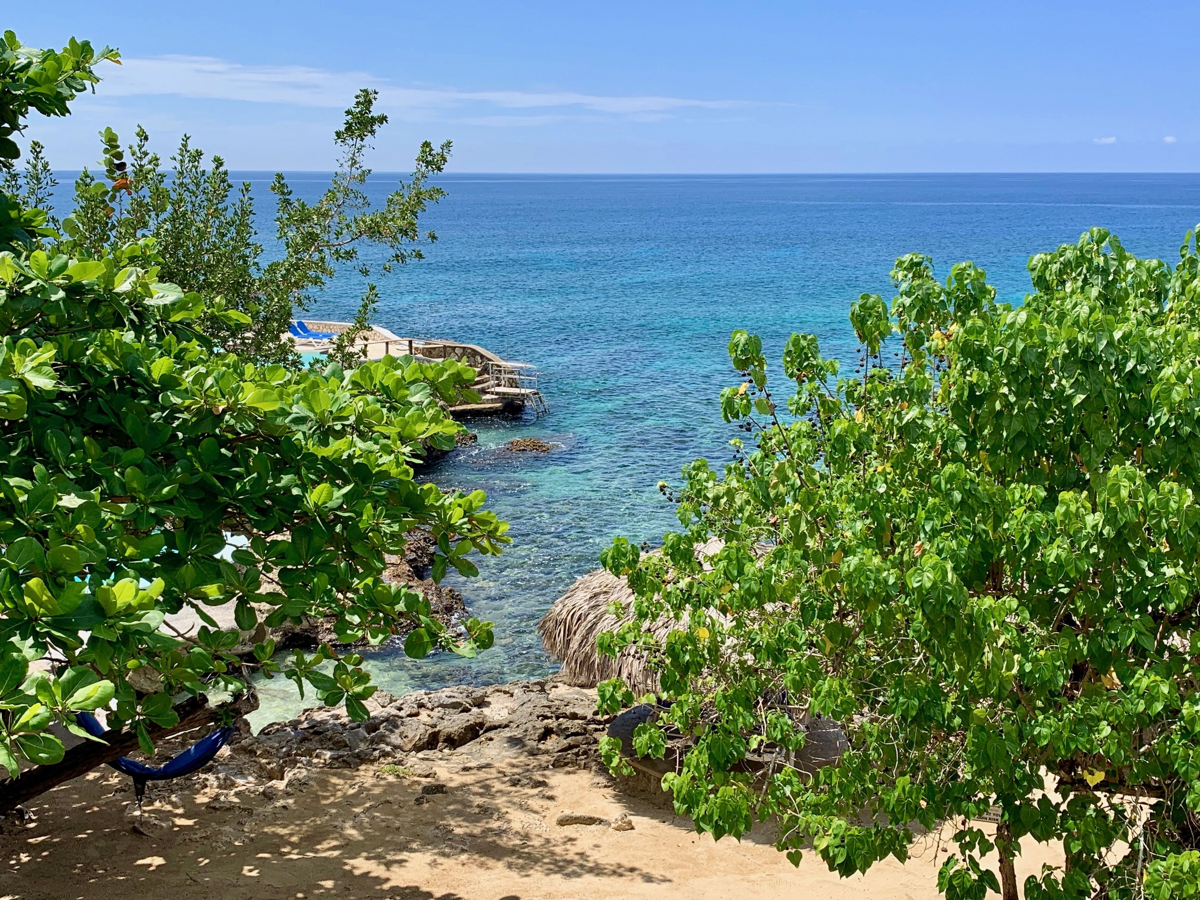Vista costeira com águas azul-claras, linha costeira rochosa e vegetação exuberante.