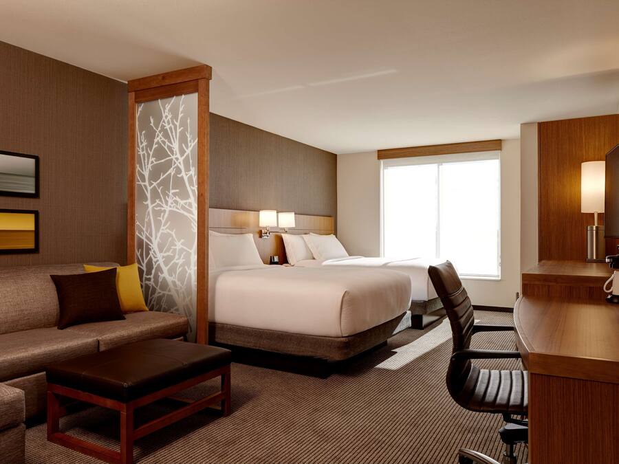 Quarto de hotel com cama, sofá, escrivaninha e televisão.