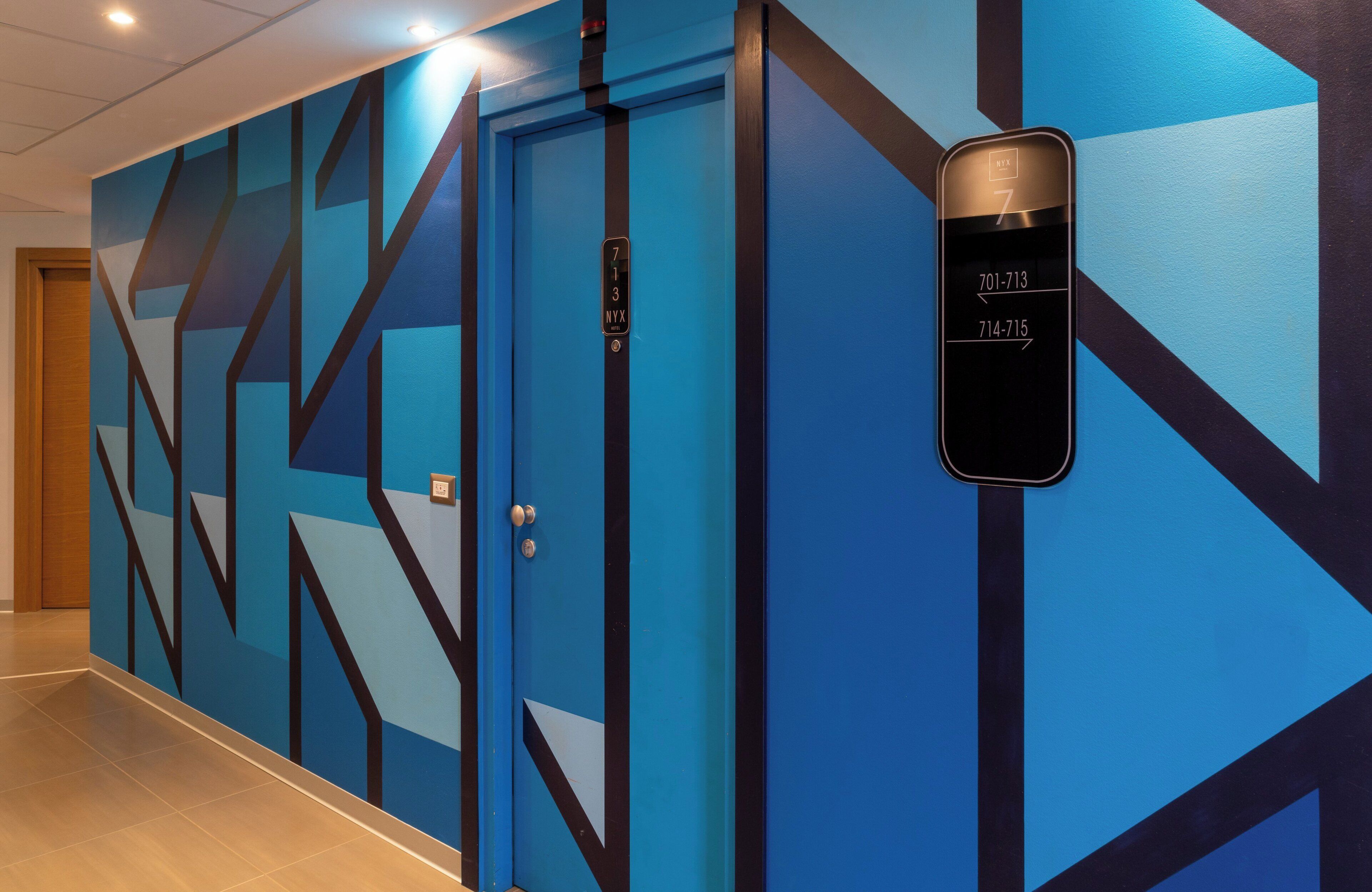 Um elevador moderno com visor digital exibindo os números dos andares e um design geométrico azul na parede.