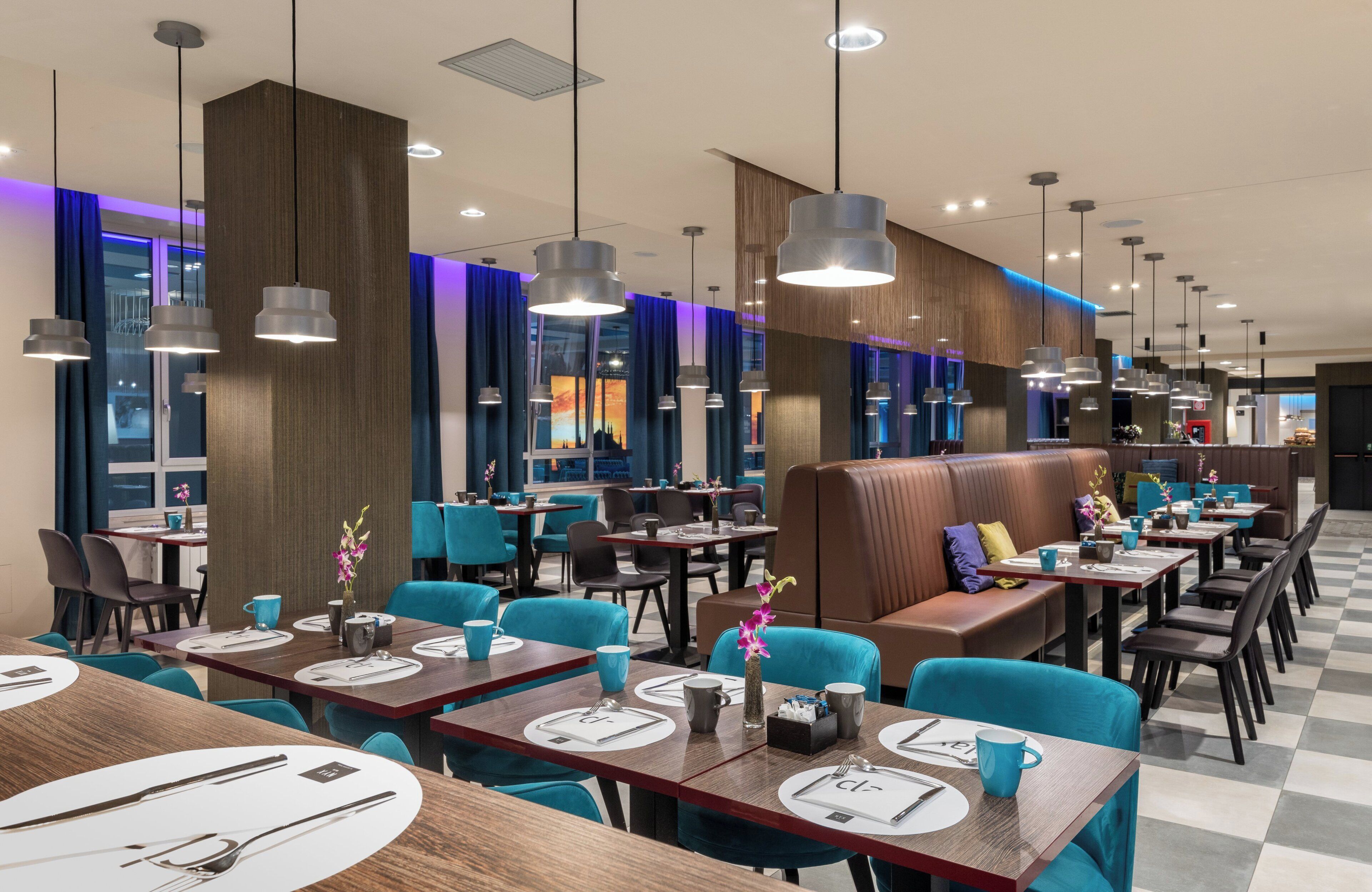 Restaurante moderno com mesas altas, cadeiras azuis e iluminação pendente.
