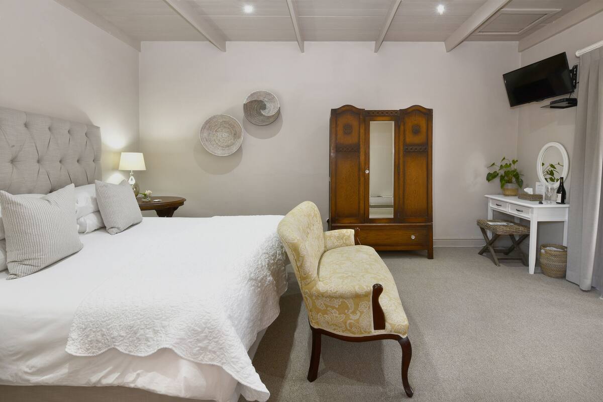 Quarto com cama, poltrona, penteadeira, televisão e espelho.