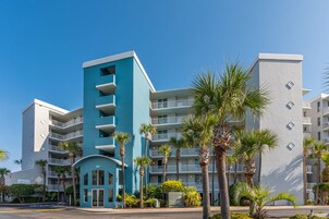 Um hotel com vários andares, fachada azul e branca, varandas e palmeiras.