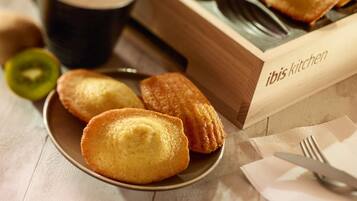 Um prato de doces, uma xícara de café e uma caixa de madeira com a etiqueta 'ibis kitchen'.