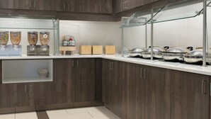 Uma cozinha moderna com armários de madeira escura, bancada branca e espaço de armazenamento com portas de vidro para alimentos.