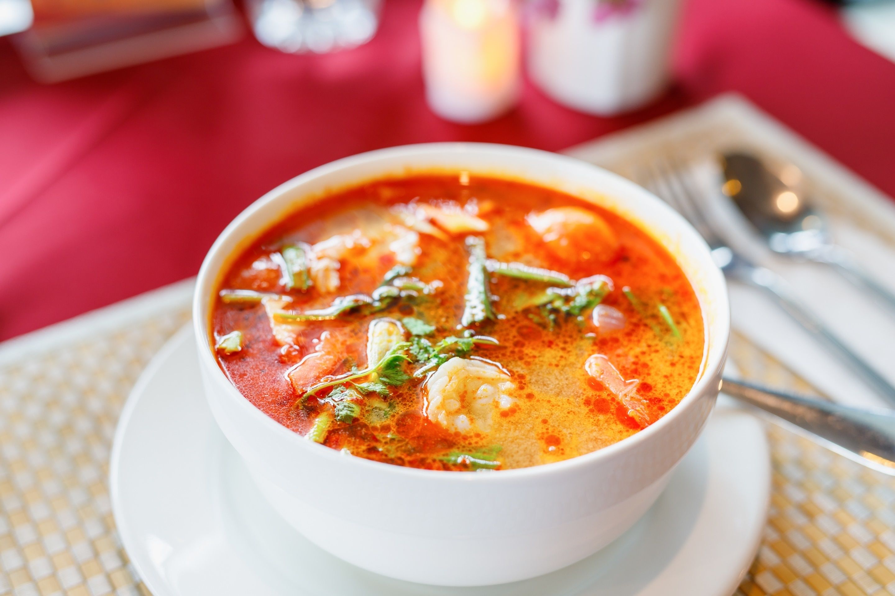 Uma tigela de sopa sobre um prato branco, com uma colher e um garfo ao lado.