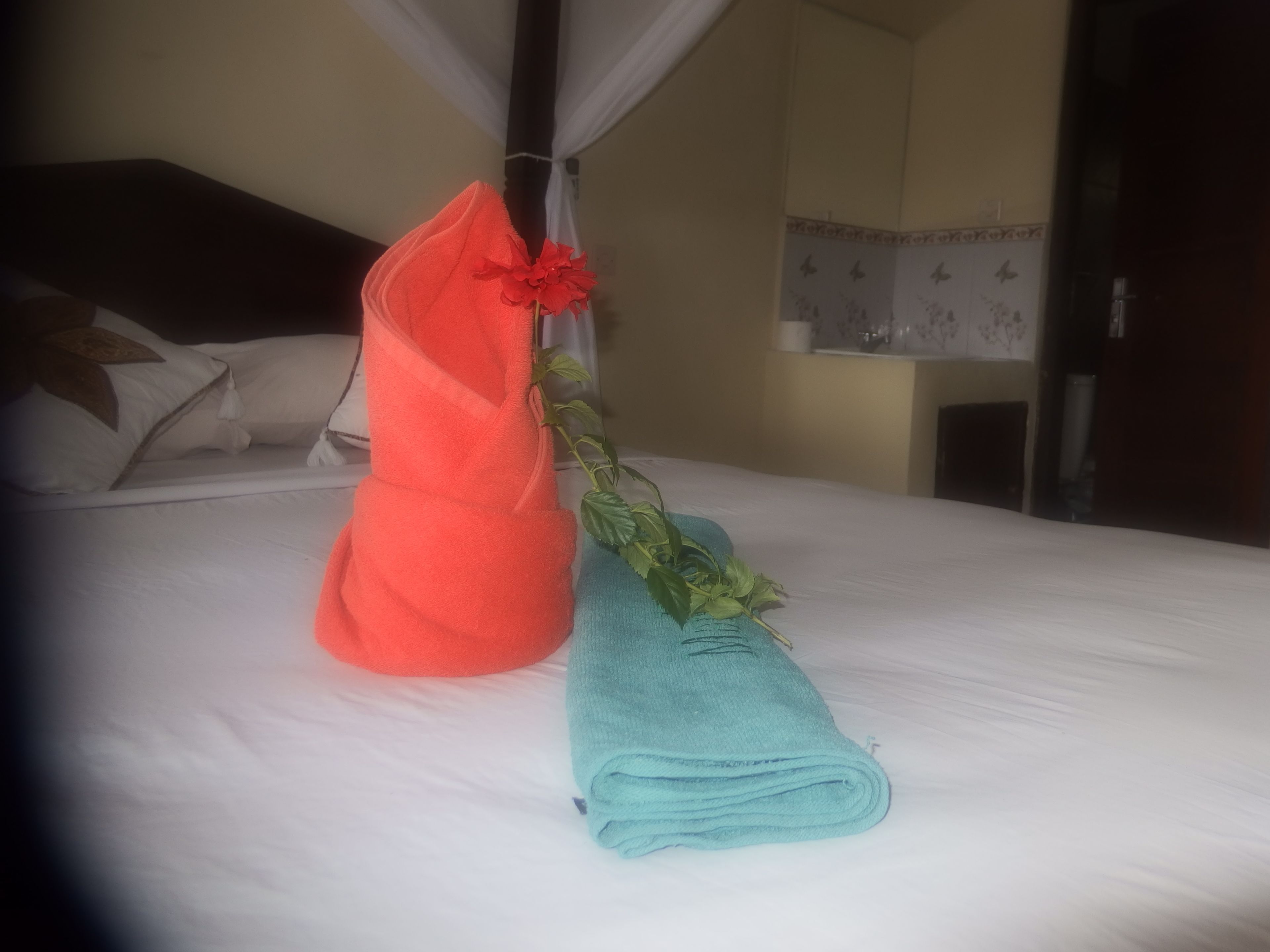 Uma cama com lençol branco, almofada vermelha e toalha azul dobrada.