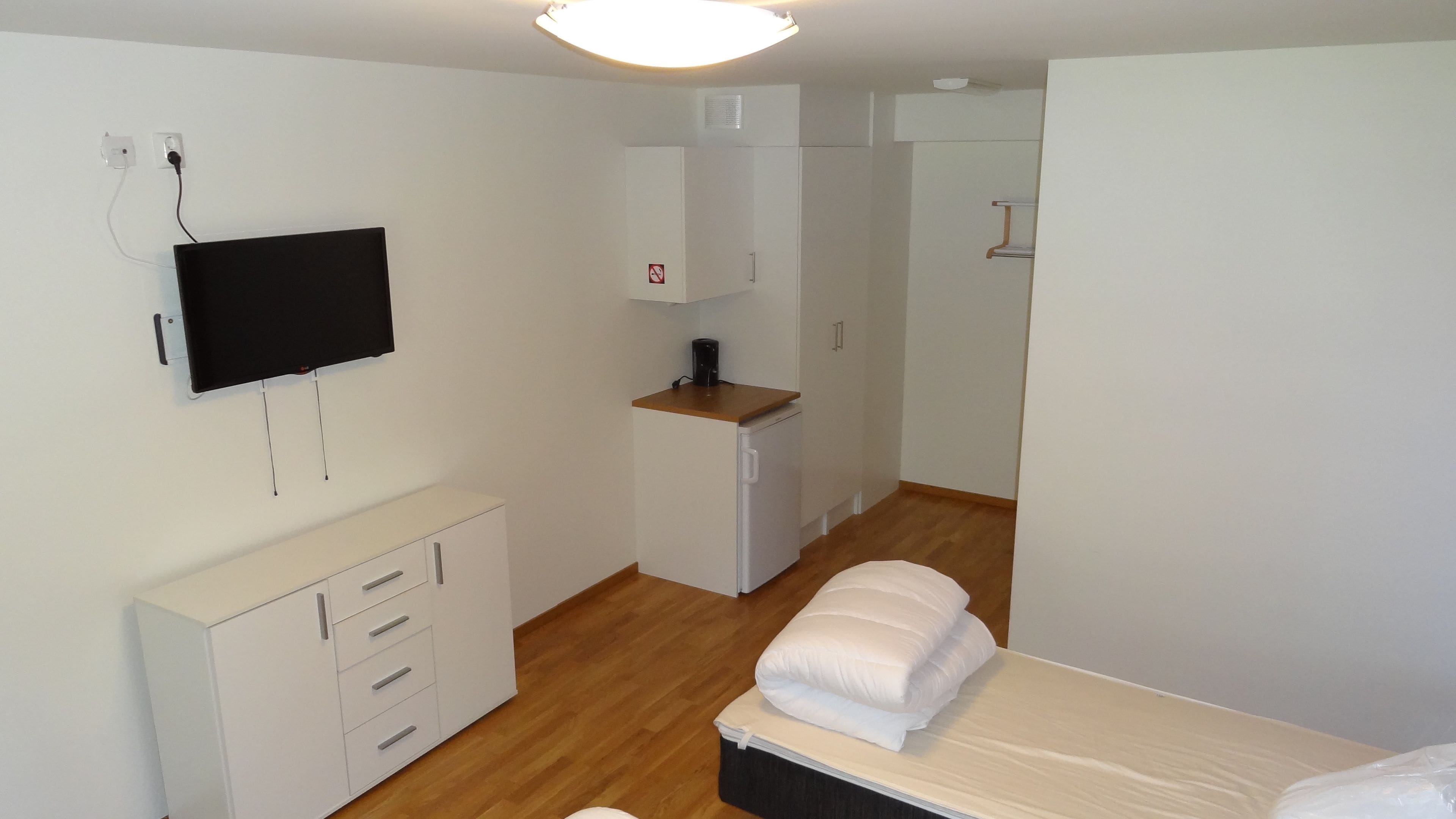 Quarto com cama, televisão, pequeno kitchenette e guarda-roupa.