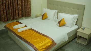 Cama bem arrumada com edredom branco e amarelo, dois travesseiros e uma toalha enrolada.
