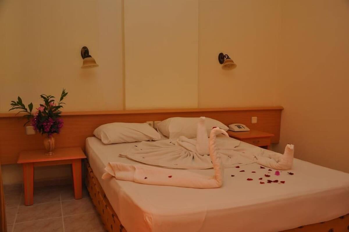 Cama bem arrumada com toalha em formato de cisne, vaso com flores na mesa de cabeceira e telefone na mesinha de dormir.