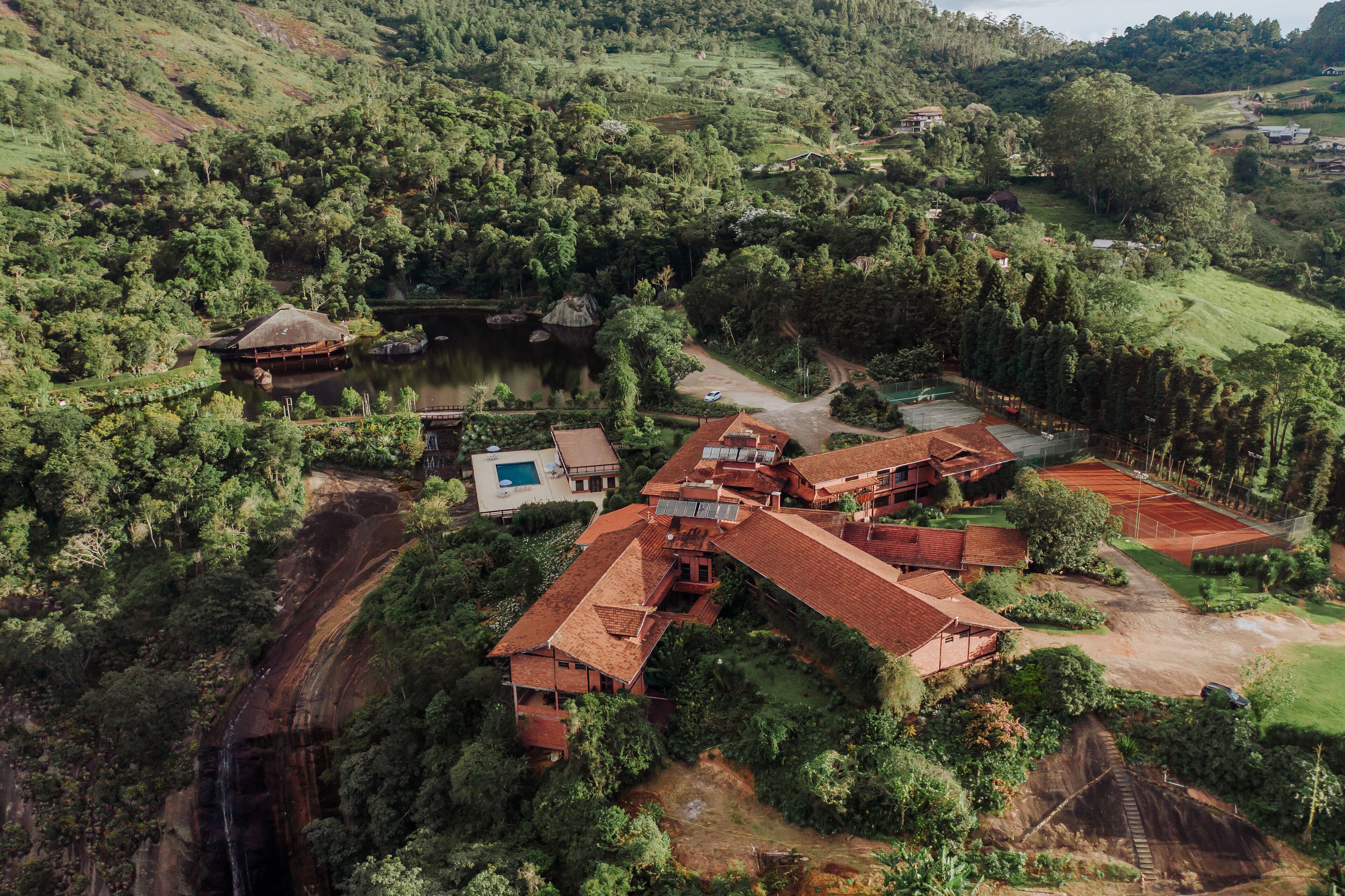 Vista aérea de um resort com vários edifícios, piscina e um lago natural rodeado por vegetação exuberante.