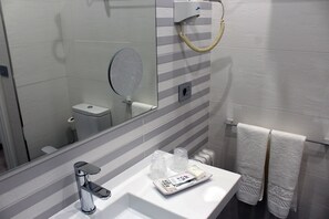 Casa de banho com lavatório branco, espelho, porta-toalhas e sanita.