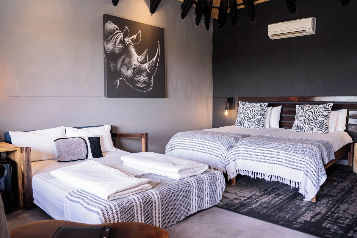 Quarto de hotel moderno com duas camas, uma grande obra de arte de um rinoceronte e ar condicionado instalado.