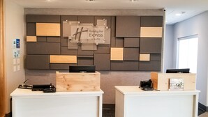 Uma área de recepção com um letreiro Holiday Inn Express, dois balcões de atendimento e uma parede com padrão geométrico.