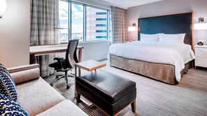 Quarto de hotel com uma cama grande, uma mesa com cadeira, uma mesinha e um sofá.