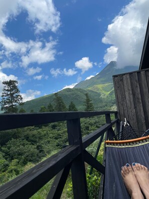 Uma rede em um deck de madeira com vista para uma paisagem verde exuberante e uma montanha ao fundo.