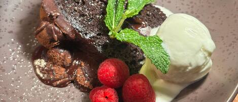 Um prato de sobremesa com um brownie, framboesas, hortelã e uma bola de sorvete.