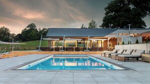 Uma área moderna de piscina ao ar livre, com piscina cristalina, espreguiçadeiras e restaurante com mesas na varanda.