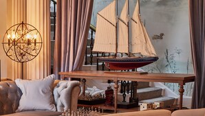 Uma sala de estar luxuosa com uma grande janela, um modelo de navio, um candelabro e um tabuleiro de xadrez.