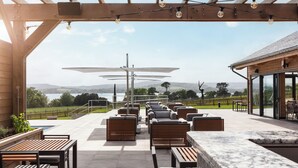 Um pátio externo com móveis de madeira, bancada de mármore e vista para a paisagem.