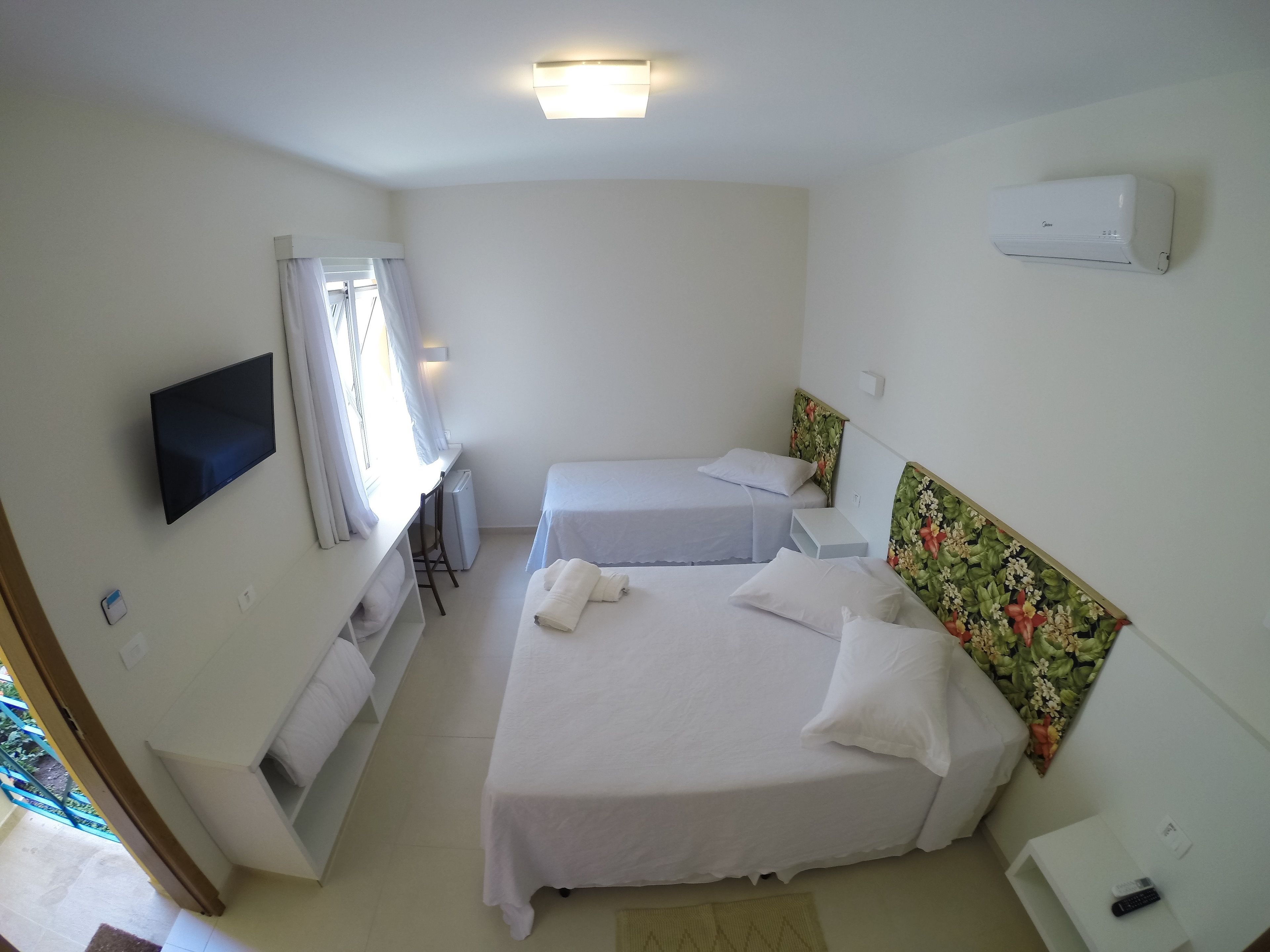 Quarto de hotel com duas camas, televisão, secretária pequena e janela com cortinas.