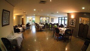 Uma sala de jantar ampla, com várias mesas e cadeiras, janelas grandes e um interior limpo e bem iluminado.