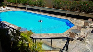 Piscina retangular com água azul cristalina, rodeada por espreguiçadeiras e uma mesa com cadeiras.