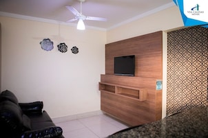 Uma sala de estar com sofá, televisão na parede, ventilador de teto e arte decorativa.
