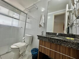 Casa de banho com sanita, lavatório, espelho e chuveiro.