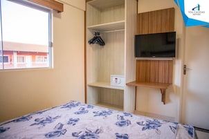 Quarto com cama, televisão na parede, guarda-roupa e janela com vista para edifícios.