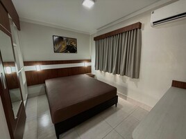 Quarto de hotel com cama, um quadro na parede, janela com cortinas e ar condicionado.