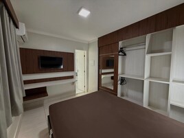 Quarto com televisão, estantes embutidas, guarda-roupa e uma cama.