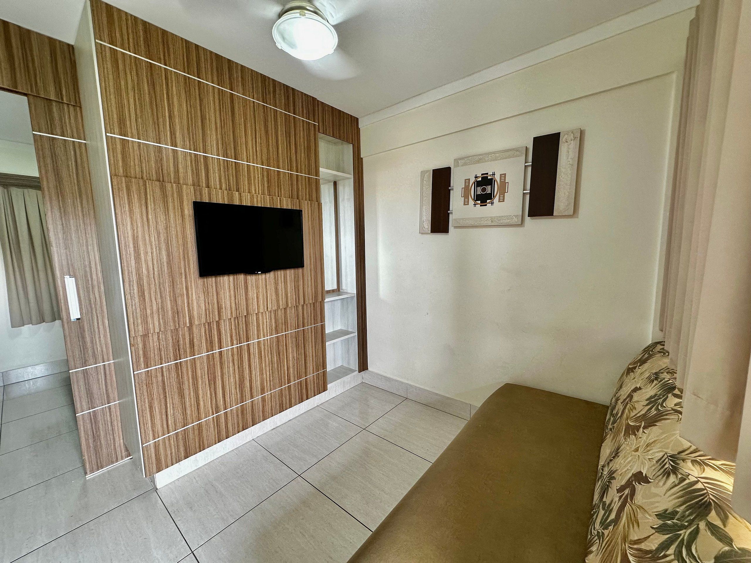 Uma sala de estar moderna com uma televisão de tela plana fixada em uma parede de painéis de madeira, um sofá estampado com flores e uma pequena mesa.
