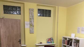 Um quarto com uma mesa de madeira, cadeiras vermelhas, uma estante e um radiador.