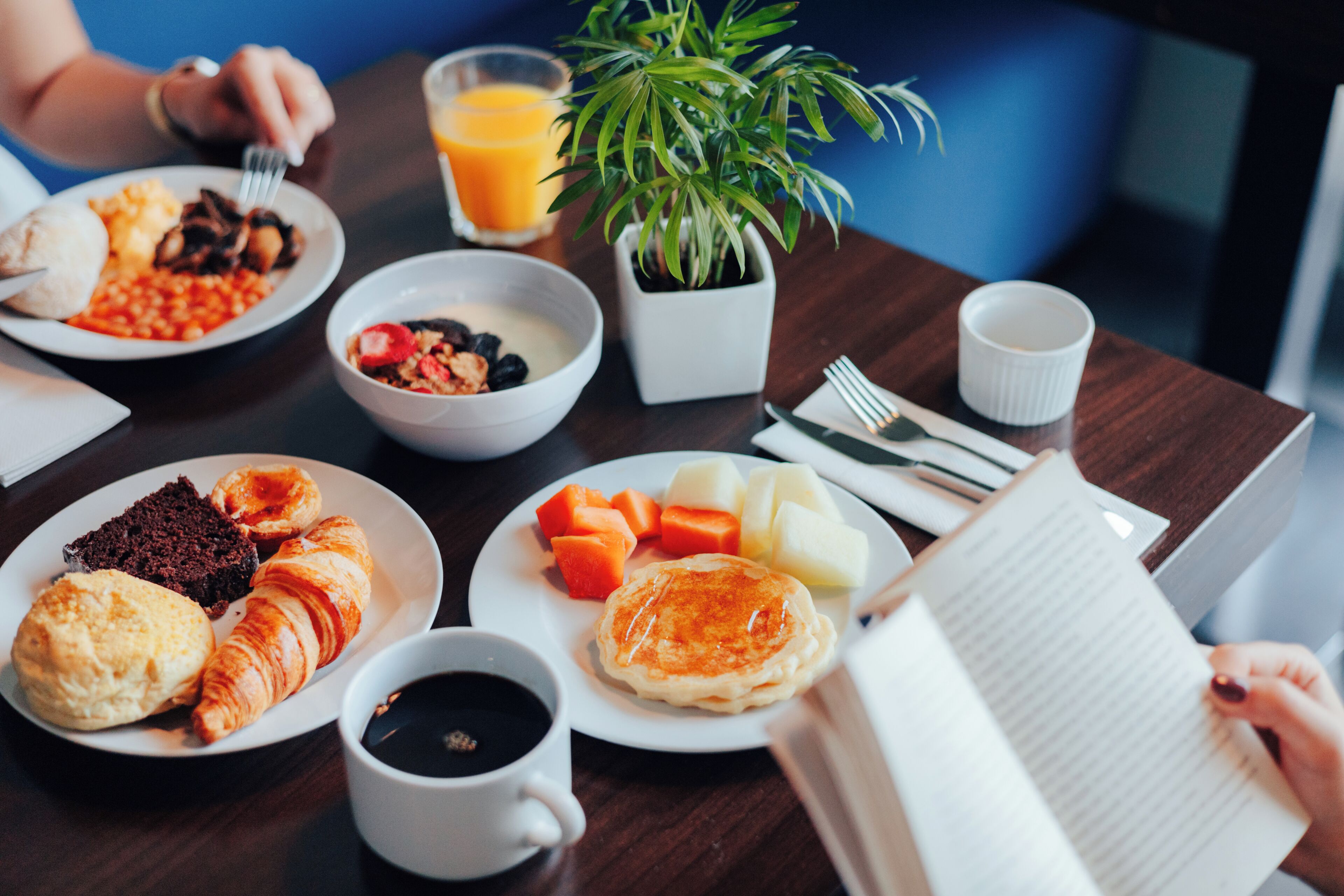 Uma mesa de café da manhã com pratos de comida, uma xícara de café e um livro.