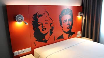 Quarto de hotel com uma cama, luminária na parede e tomada.