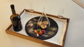 Uma bandeja com uma garrafa de vinho, duas taças e um prato com doces e morangos.