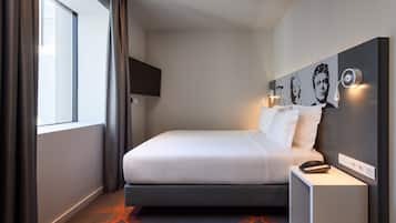 Quarto de hotel moderno com uma cama grande, uma mesa de cabeceira com telefone e uma TV fixada na parede.