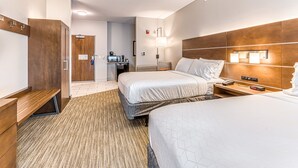 Quarto de hotel com duas camas, guarda-roupa de madeira, escrivaninha, abajur e uma pequena mesa com telefone e relógio.
