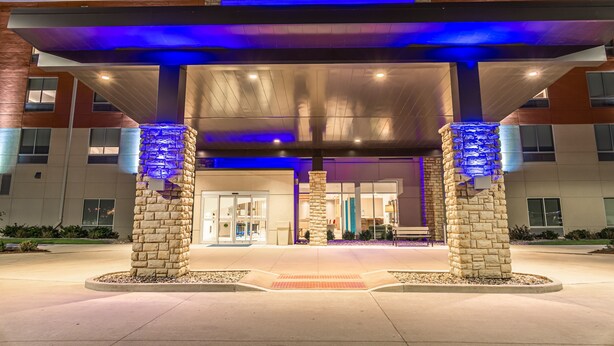 Entrada de hotel com design moderno, apresentando uma galeria coberta e pilares de pedra.