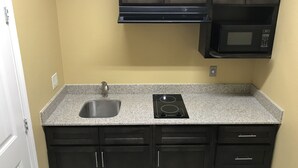 Cozinha compacta com bancada de granito, pia de aço inoxidável, armários pretos, micro-ondas e fogão por indução.