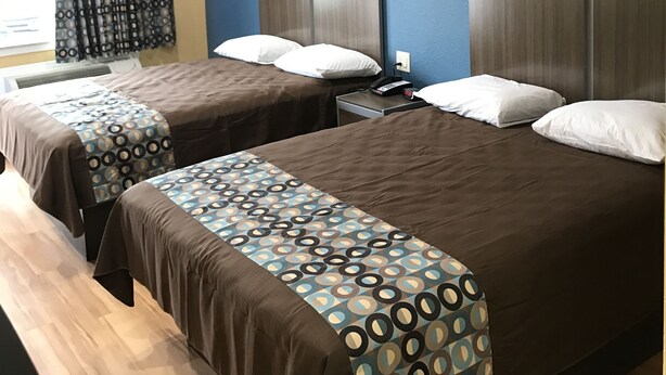 Quarto de hotel com duas camas, uma mesinha de cabeceira e uma janela com cortinas.