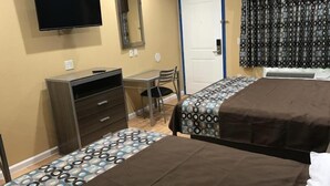 Quarto de hotel com cama, escrivaninha, cadeira, televisão e tapete estampado.
