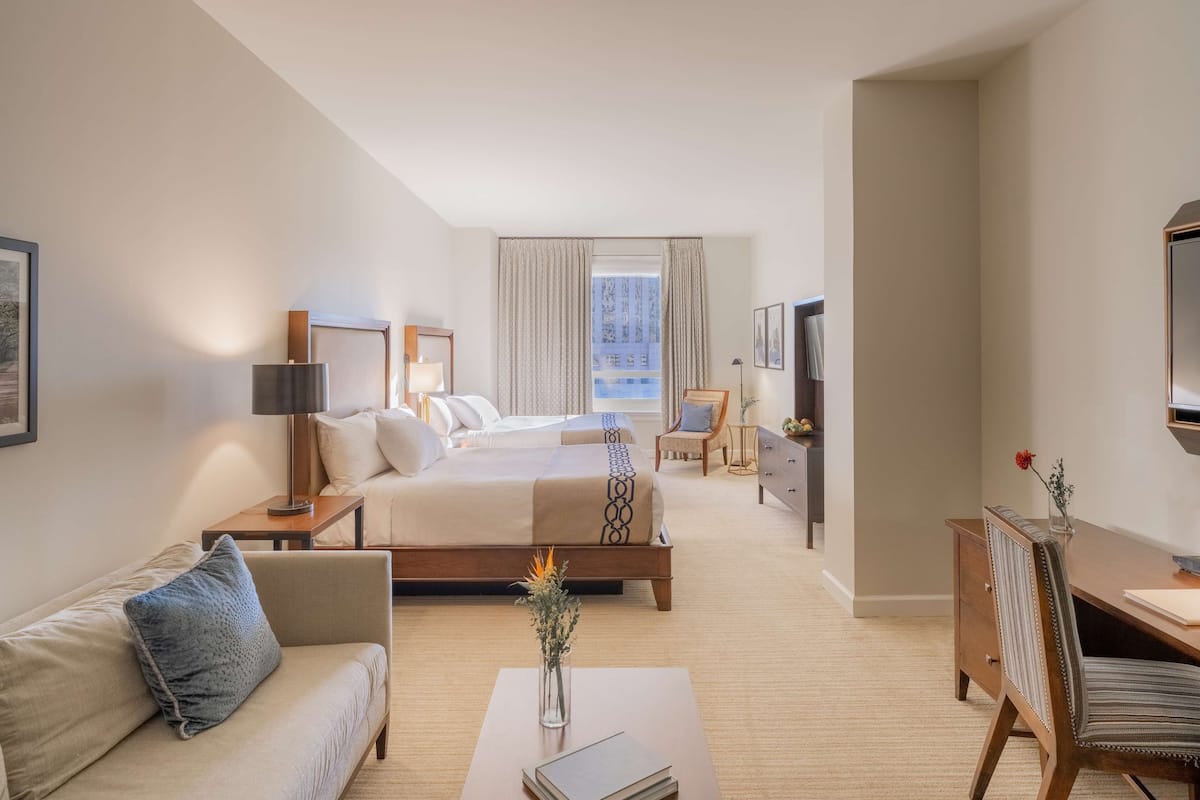 Quarto de hotel com cama, sofá, escrivaninha e televisão.