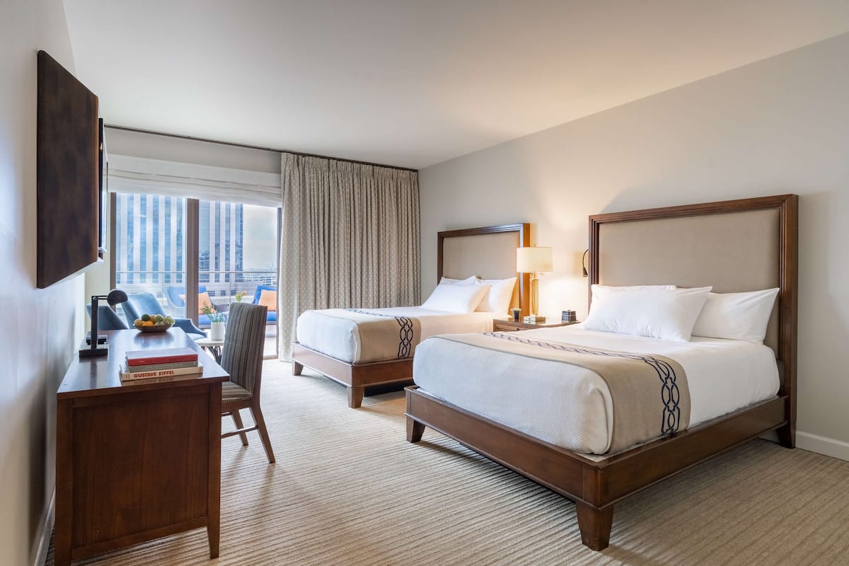 Quarto de hotel com duas camas, uma escrivaninha e uma cadeira.