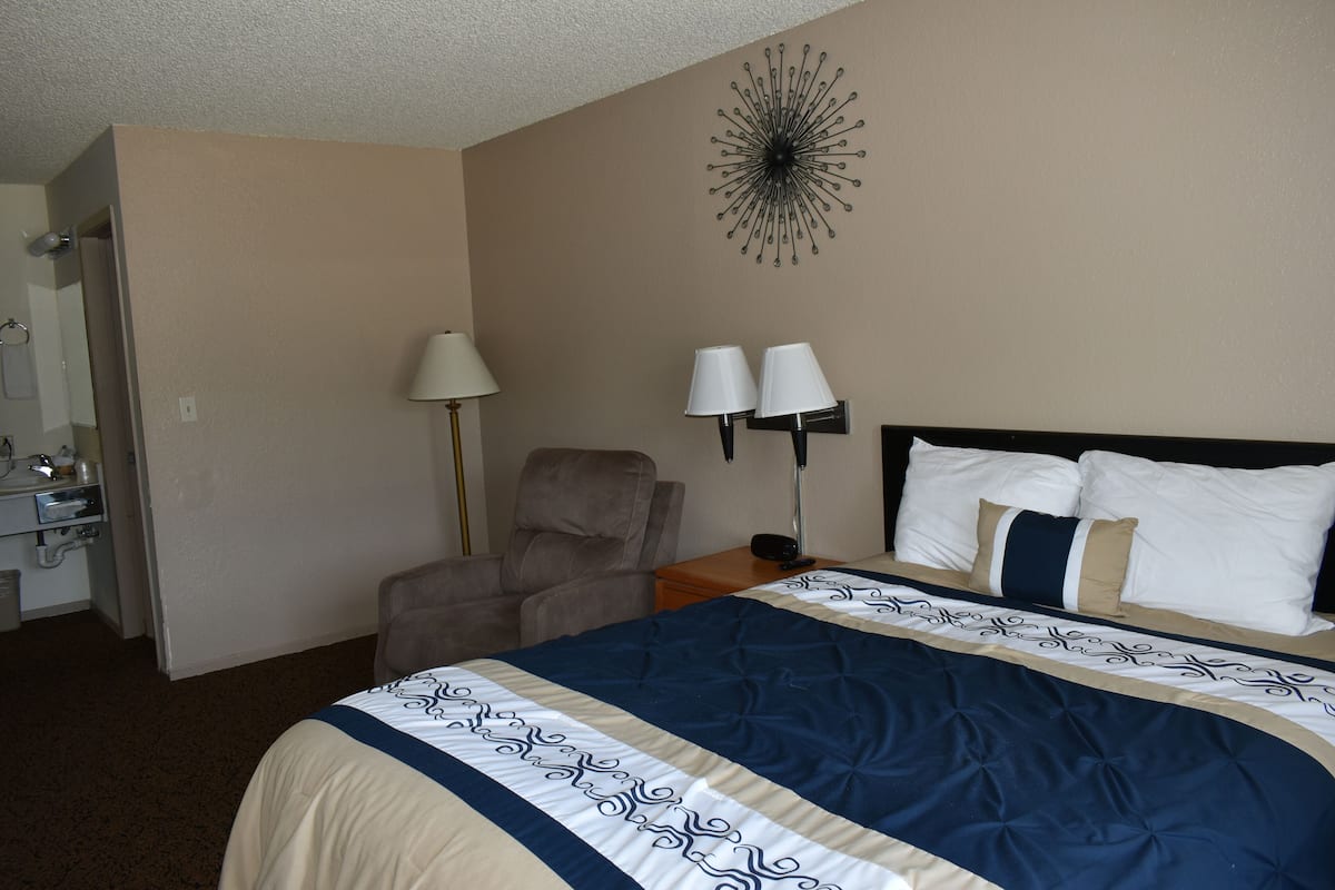 Quarto de hotel com uma cama, duas luminárias de cabeceira, uma cadeira e um banheiro visível ao fundo.